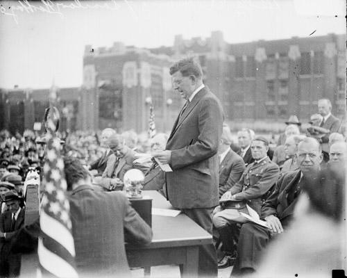 ECC | [Edward J. Kelly standing at a podium in front of a building