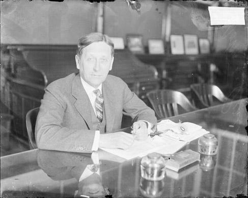 ECC | [John T. Pirie resting both hands on a table, looking toward