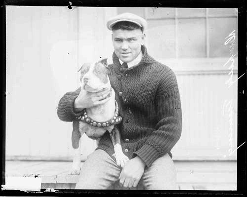 ECC | [Boxer, Jack Dempsey holding a dog, sitting in front of a bu